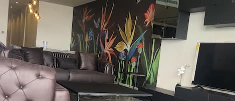 Uma sala de estar moderna com piso de mármore, sofá de couro, TV de tela plana e um mural na parede.