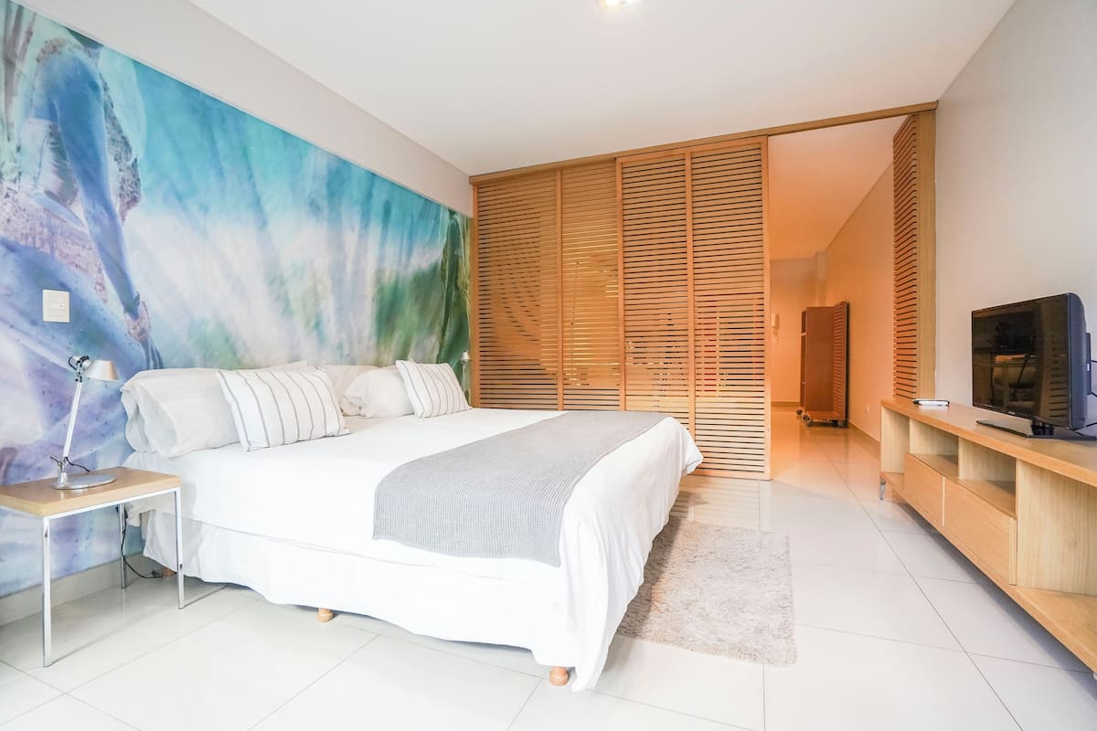 Quarto moderno com uma cama grande, uma TV e um guarda-roupa de madeira.