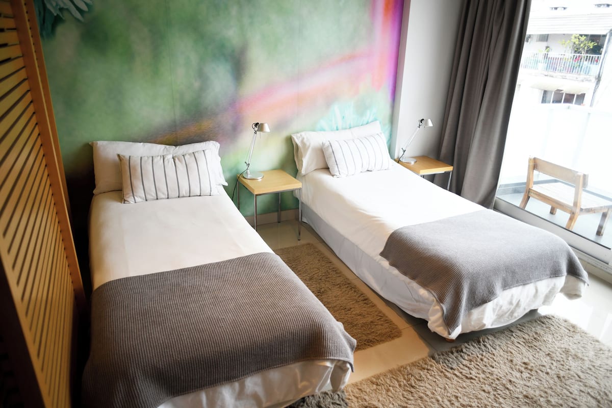 Quarto de hotel com duas camas, uma janela grande e vista para o exterior.