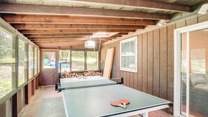 Mesa de pingue-pongue em um quarto de madeira com janelas amplas e uma porta que dá para o exterior.