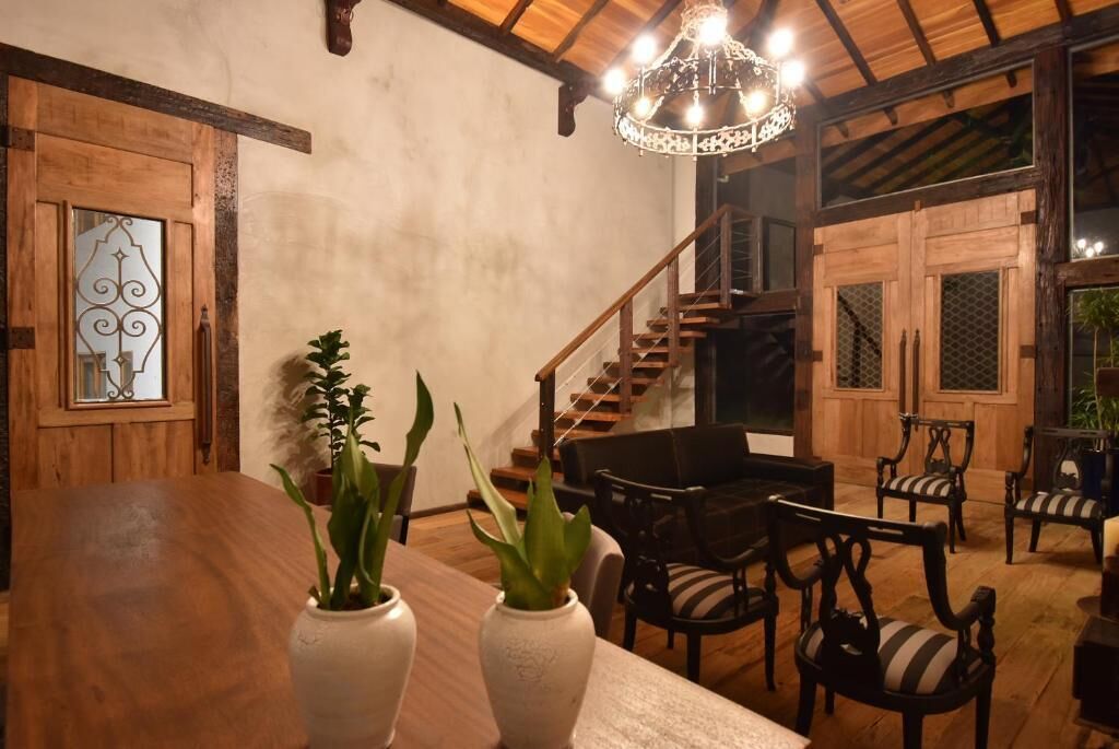 Uma área de refeições de madeira com uma mesa grande, duas plantas em vasos e um candelabro.