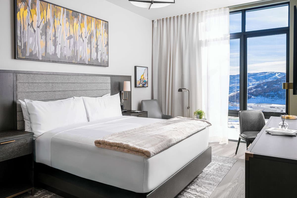 Quarto de hotel moderno com uma cama grande, uma escrivaninha e vista para uma paisagem nevada.