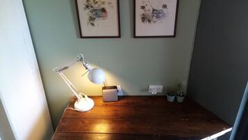 Uma mesa de madeira com uma luminária de mesa branca, duas obras de arte emolduradas na parede, uma tomada e dois pequenos vasos com plantas.