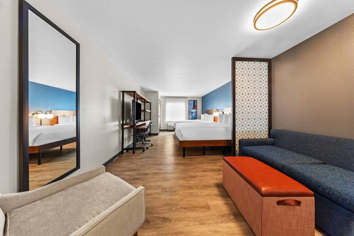 Quarto de hotel com uma cama grande, uma escrivaninha com cadeira, um sofá e um pequeno banquinho.