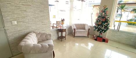 Uma sala de estar espaçosa, com uma grande janela, um pinheiro de Natal e duas poltronas.