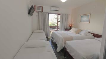 Quarto de hotel com duas camas de solteiro, televisão, ar condicionado, janela com cortinas e uma pequena mesa com luminária.