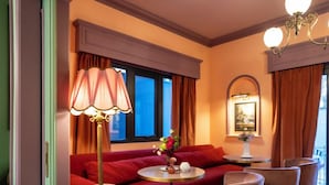 Quarto acolhedor com um sofá vermelho, uma mesa redonda e cadeiras combinando. Uma luminária de chão e um candelabro proporcionam iluminação.