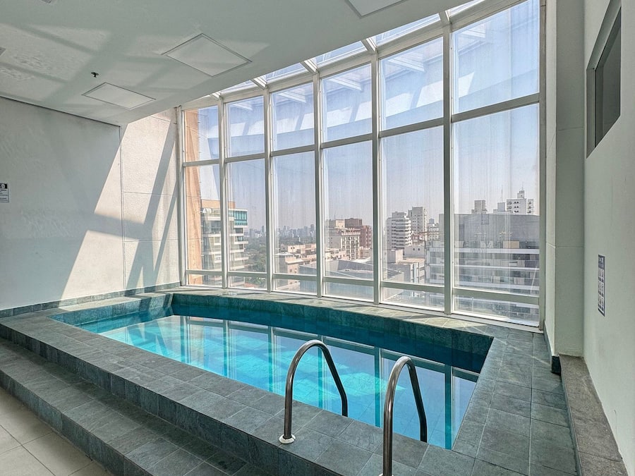 Piscina interior moderna com vista para a cidade através de grandes janelas.
