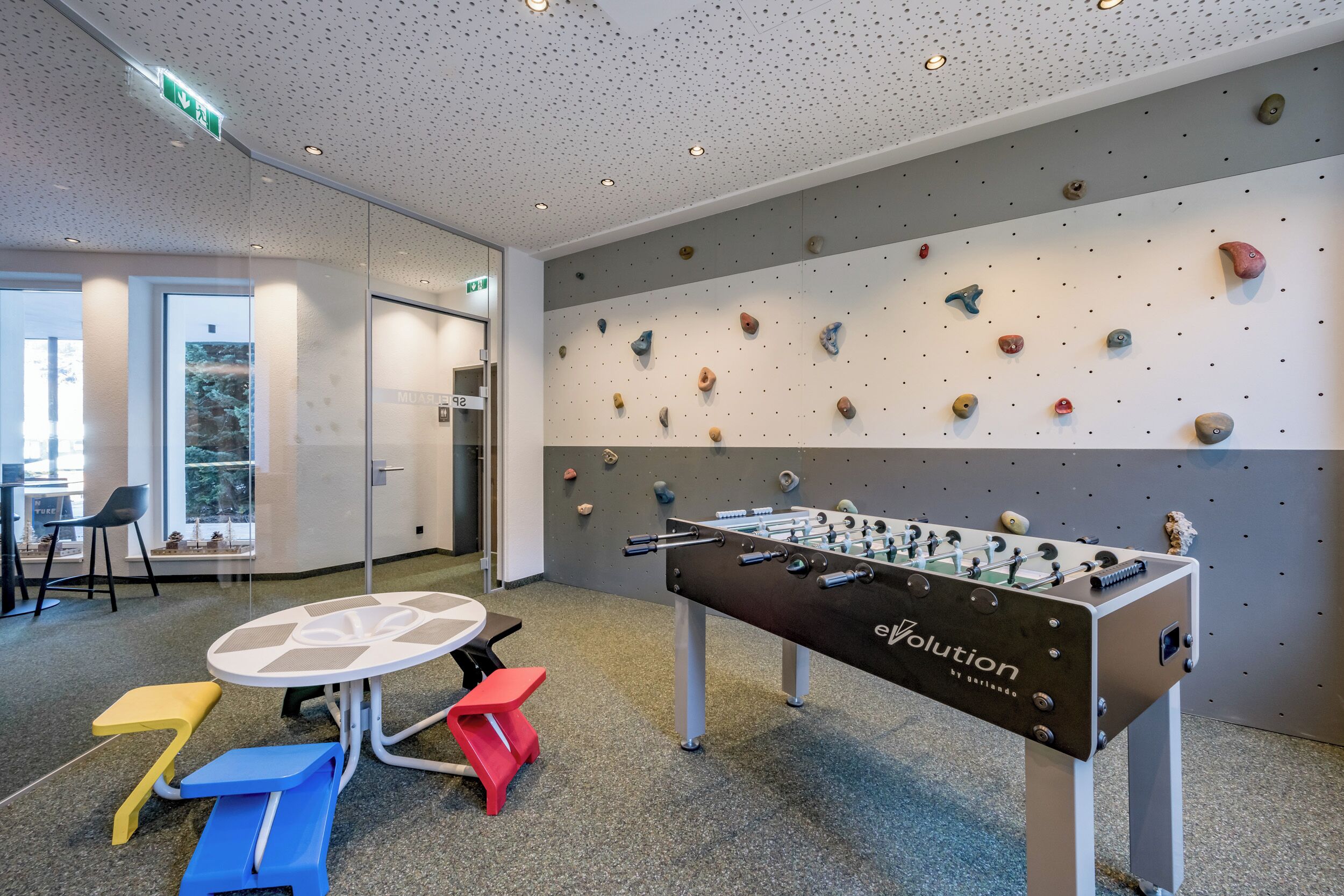 Espaço interior moderno com mesa de pebolim, parede de escalada e área de estar.
