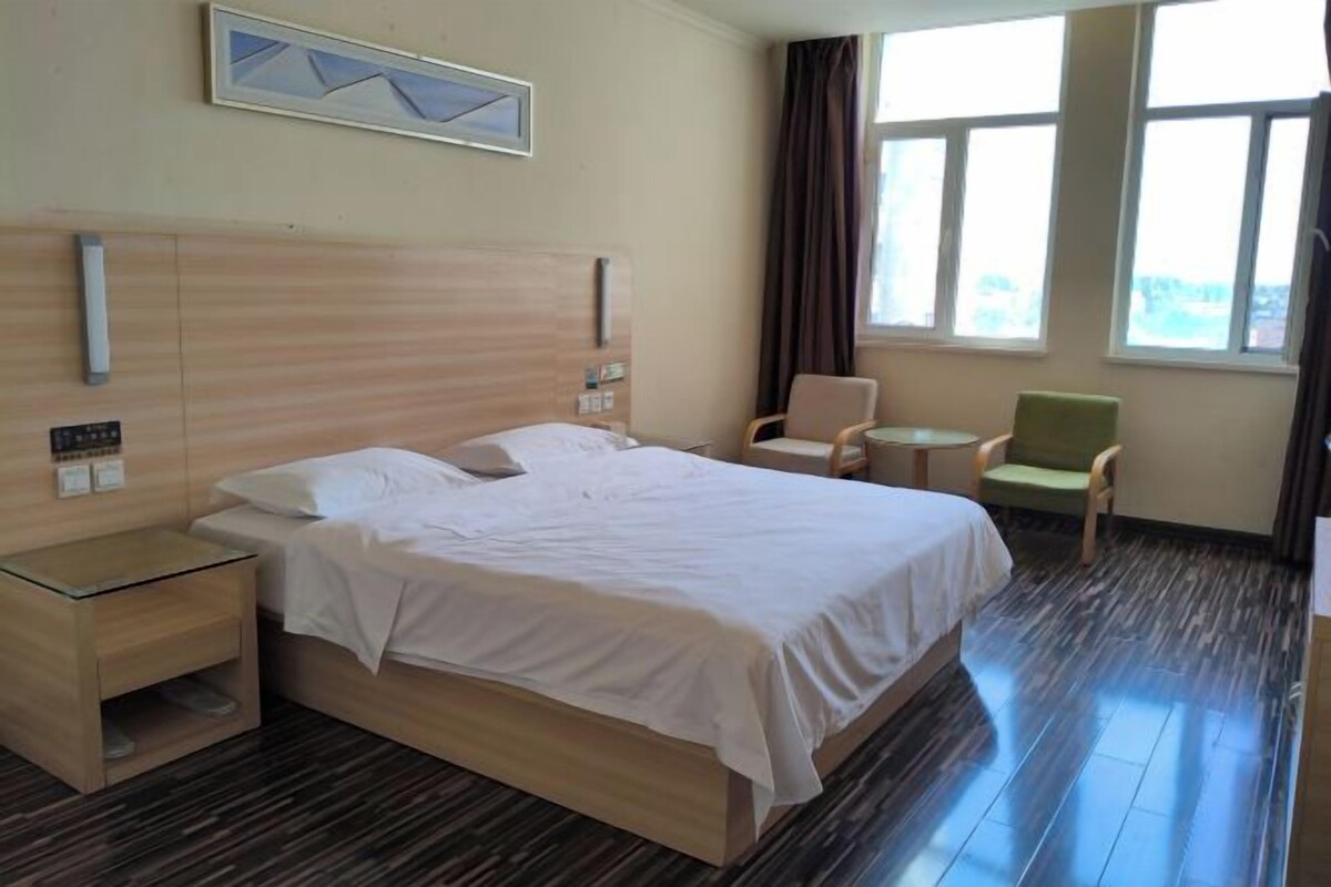 Quarto de hotel com cama grande, mesas de cabeceira, uma cadeira, mesinha e janela.