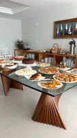 Uma mesa de buffet com diversos alimentos, um espaço para café e uma área de estar com cadeiras.