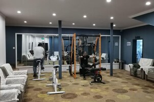 Academia com equipamentos de exercício, espelho e áreas de estar.
