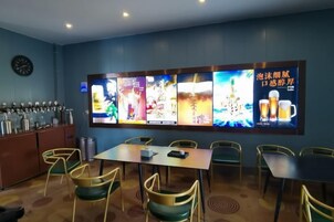 Interior de restaurante com mesas, cadeiras, área de bar e um grande painel digital de cardápio.