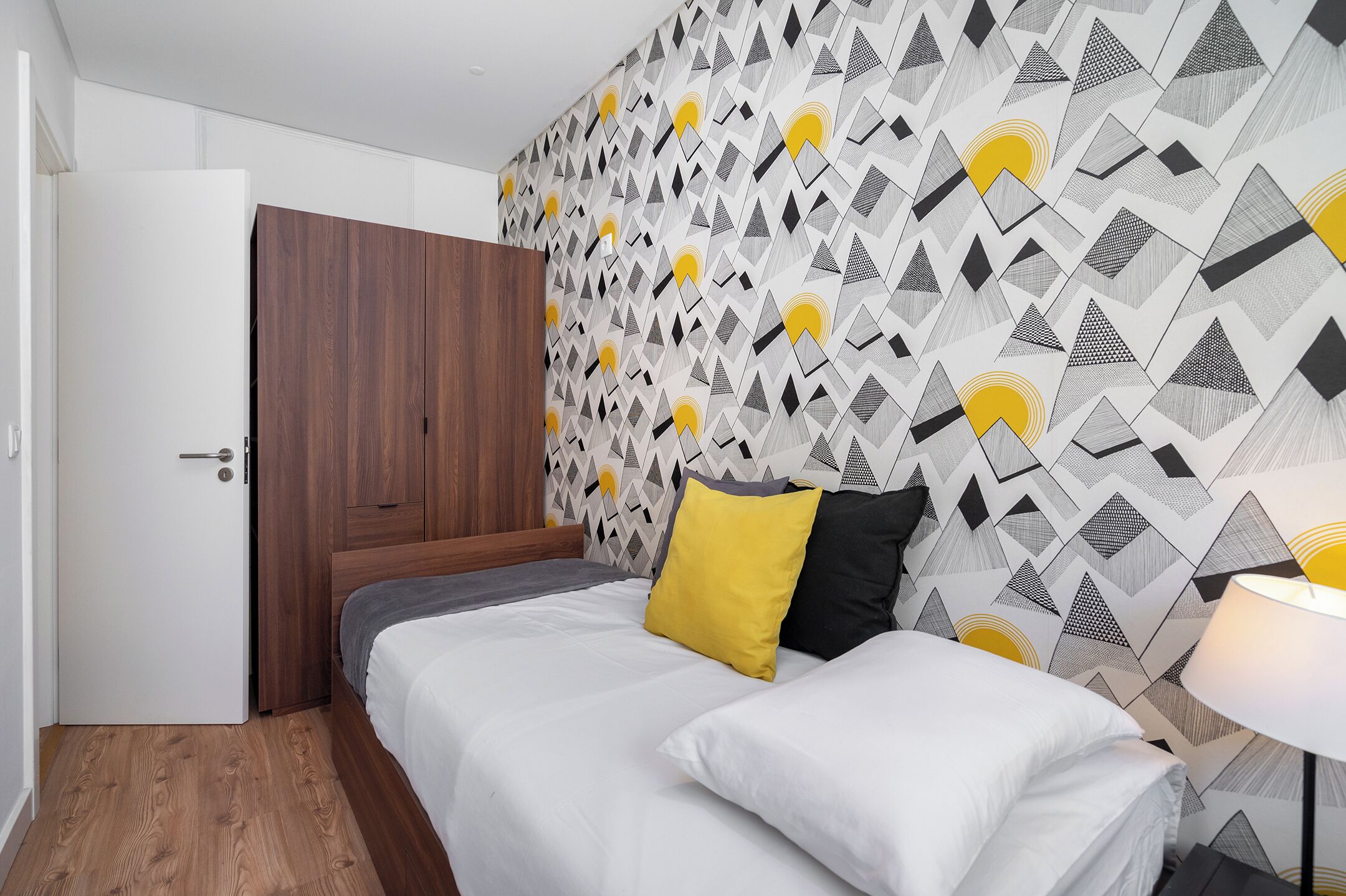 Quarto com uma cama, um guarda-roupa de madeira e parede estampada.