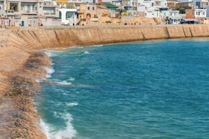 Vista costeira com um muro marítimo e edifícios ao fundo.