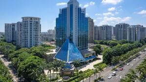 Um moderno edifício alto com estrutura em forma de pirâmide, rodeado por palmeiras e outros edifícios altos.