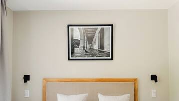 Quarto com cama, duas almofadas, cabeceira de madeira e uma fotografia emoldurada na parede.