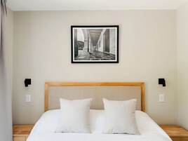 Quarto com cama, duas almofadas, cabeceira de madeira e uma fotografia emoldurada na parede.