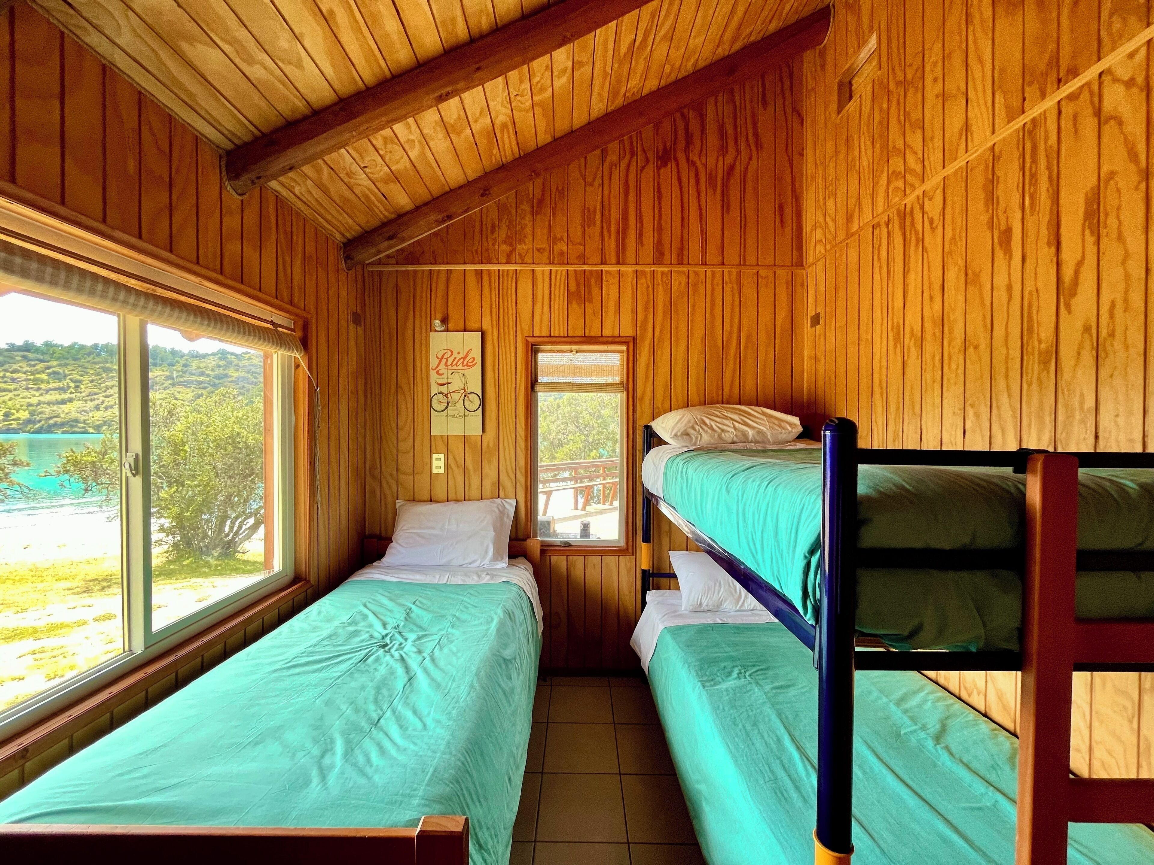 Uma cabana de madeira com beliches, uma janela com vista para a praia e uma placa na parede.