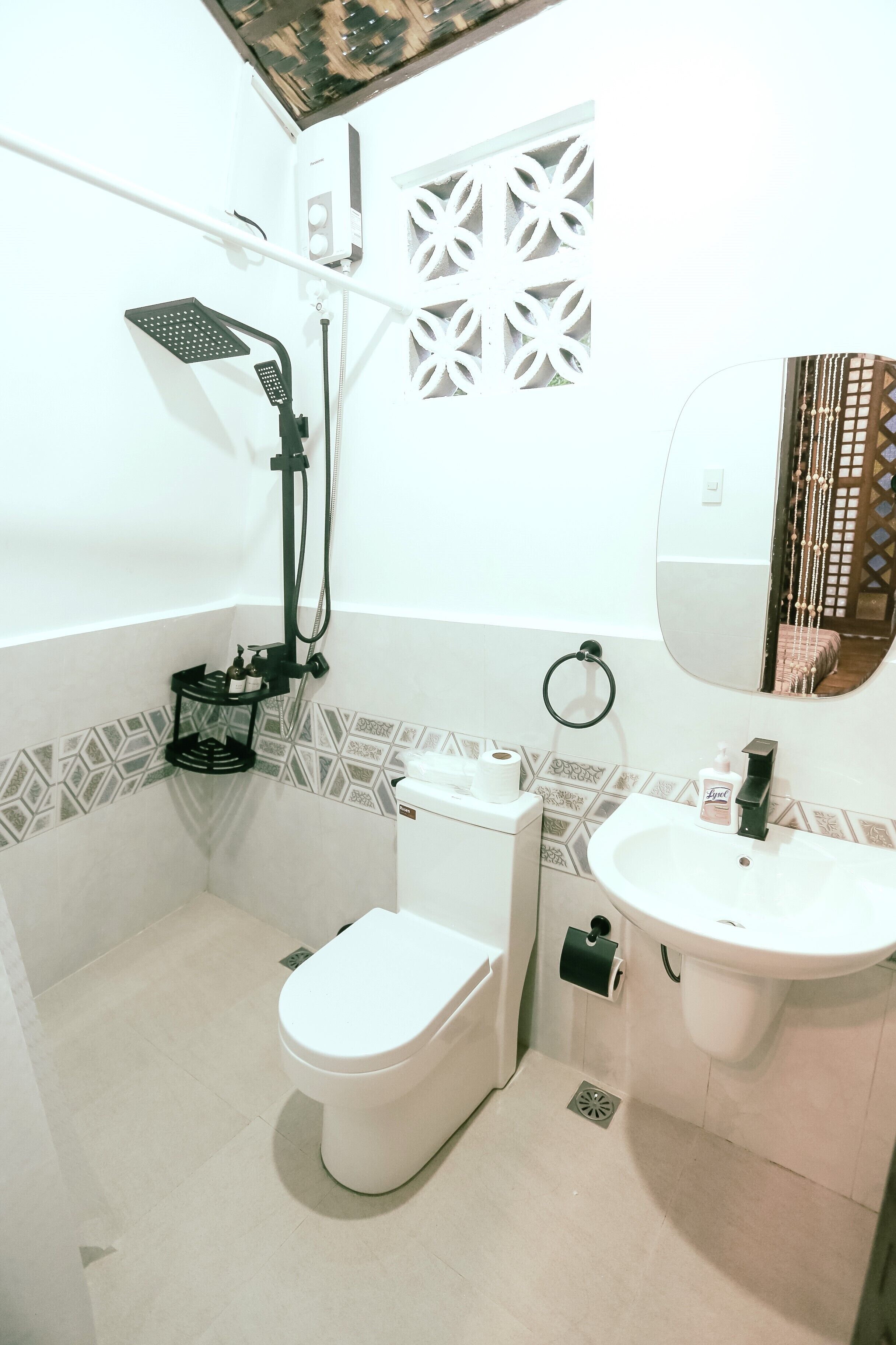 Casa de banho com sanita, lavatório, chuveiro e azulejos decorativos.