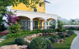 Um edifício amarelo com varanda coberta, lago e paisagismo tropical.