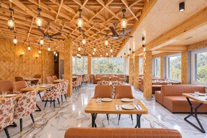 Restaurante com vigas de madeira no teto, iluminação pendente e piso de mármore. Mesas e cabines dispostas para refeições.