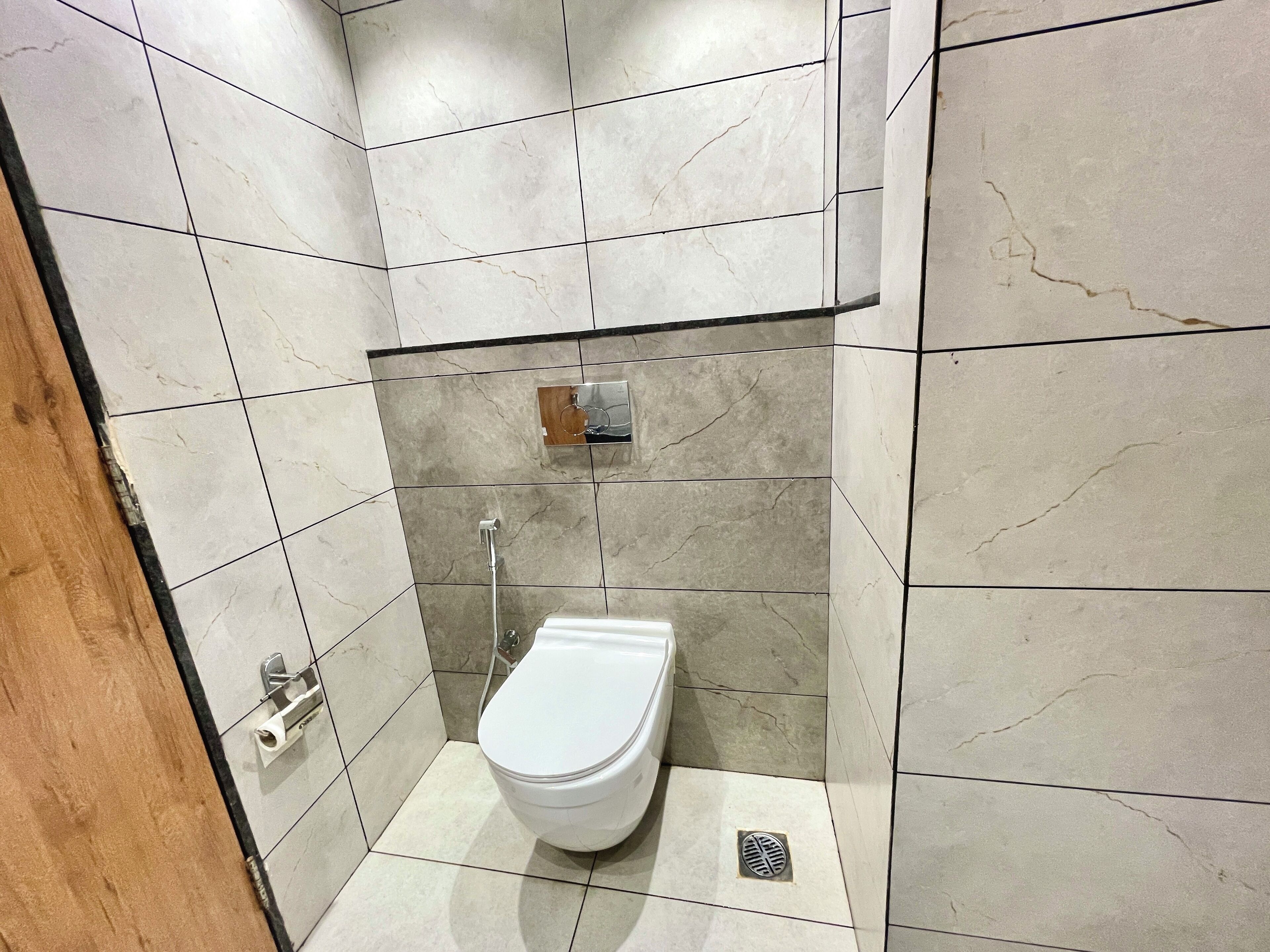 Casa de banho pequena, com azulejos, vaso sanitário, chuveiro e secador de mãos.