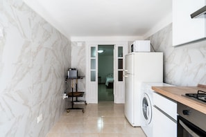 Cozinha compacta com máquina de lavar, micro-ondas e bancada de madeira.