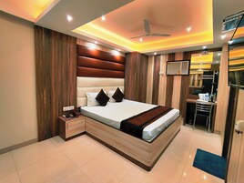 Quarto moderno com cama grande, painéis de madeira, ventilador de teto e uma pequena mesa de cabeceira.