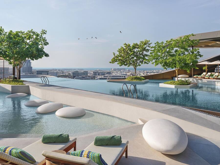 Piscina infinita no terraço com espreguiçadeiras e vista para a cidade.