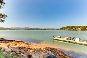 Um cais à beira do lago com um barco, água calma e colinas ao longe.
