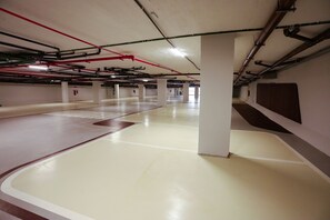 Garagem de estacionamento vazia com pisos brancos, canos vermelhos e pretos no teto e pilares brancos.