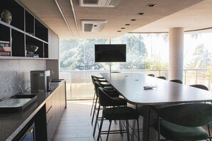 Uma sala de conferência moderna com uma mesa comprida, cadeiras, uma TV de tela plana e uma janela grande com vista para árvores.