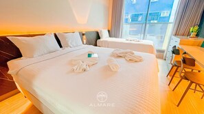 Quarto de hotel com uma cama grande, duas camas menores, uma escrivaninha e uma cadeira.