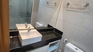 Casa de banho moderna com lavatório branco, bancada preta e sanita.