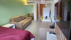 Quarto de hotel moderno com uma cama grande, um sofá, uma escrivaninha com computador e uma televisão.