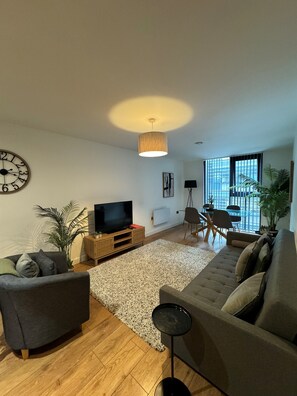 Uma sala de estar moderna com televisão de tela plana, sofá, mesa de centro e uma área de jantar com cadeiras.
