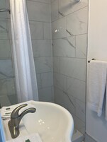 Uma casa de banho com uma banheira branca, um chuveiro com porta de vidro e uma toalha branca pendurada na parede.