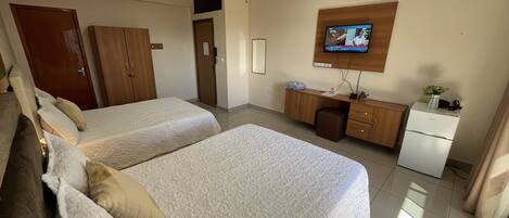 Quarto de hotel com duas camas, uma escrivaninha, um refrigerador e uma televisão na parede.
