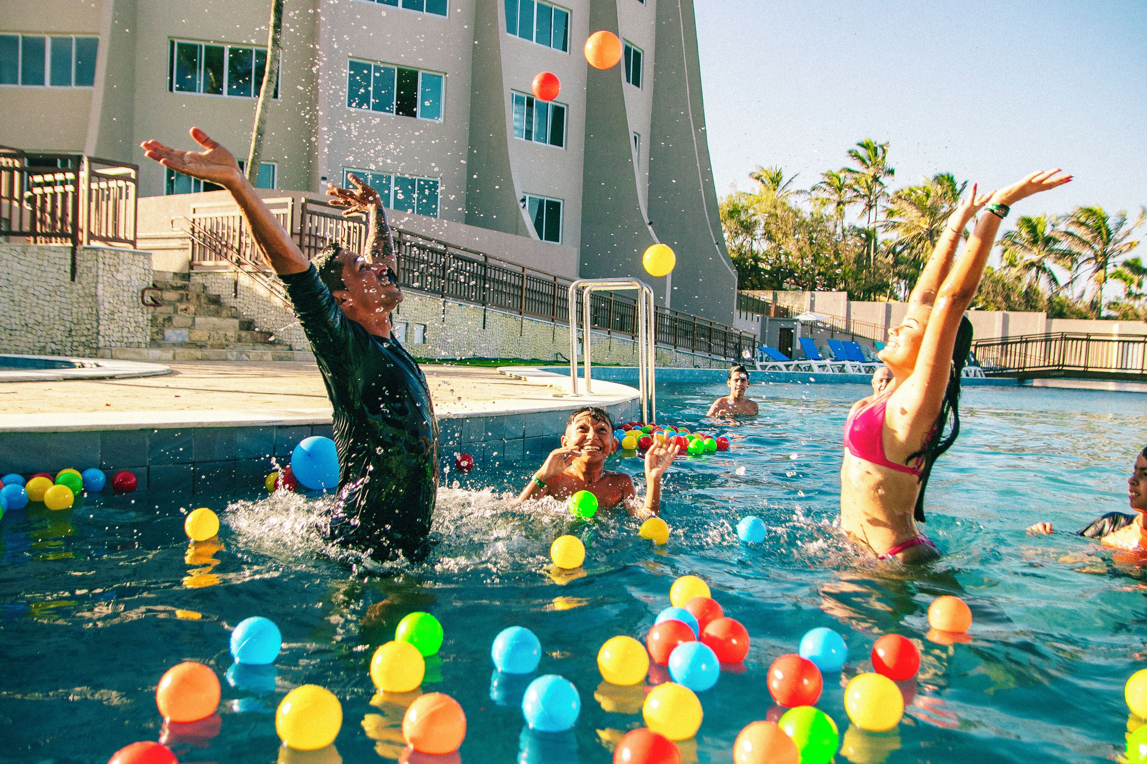 Piscina com balões coloridos e pessoas aproveitando a água.