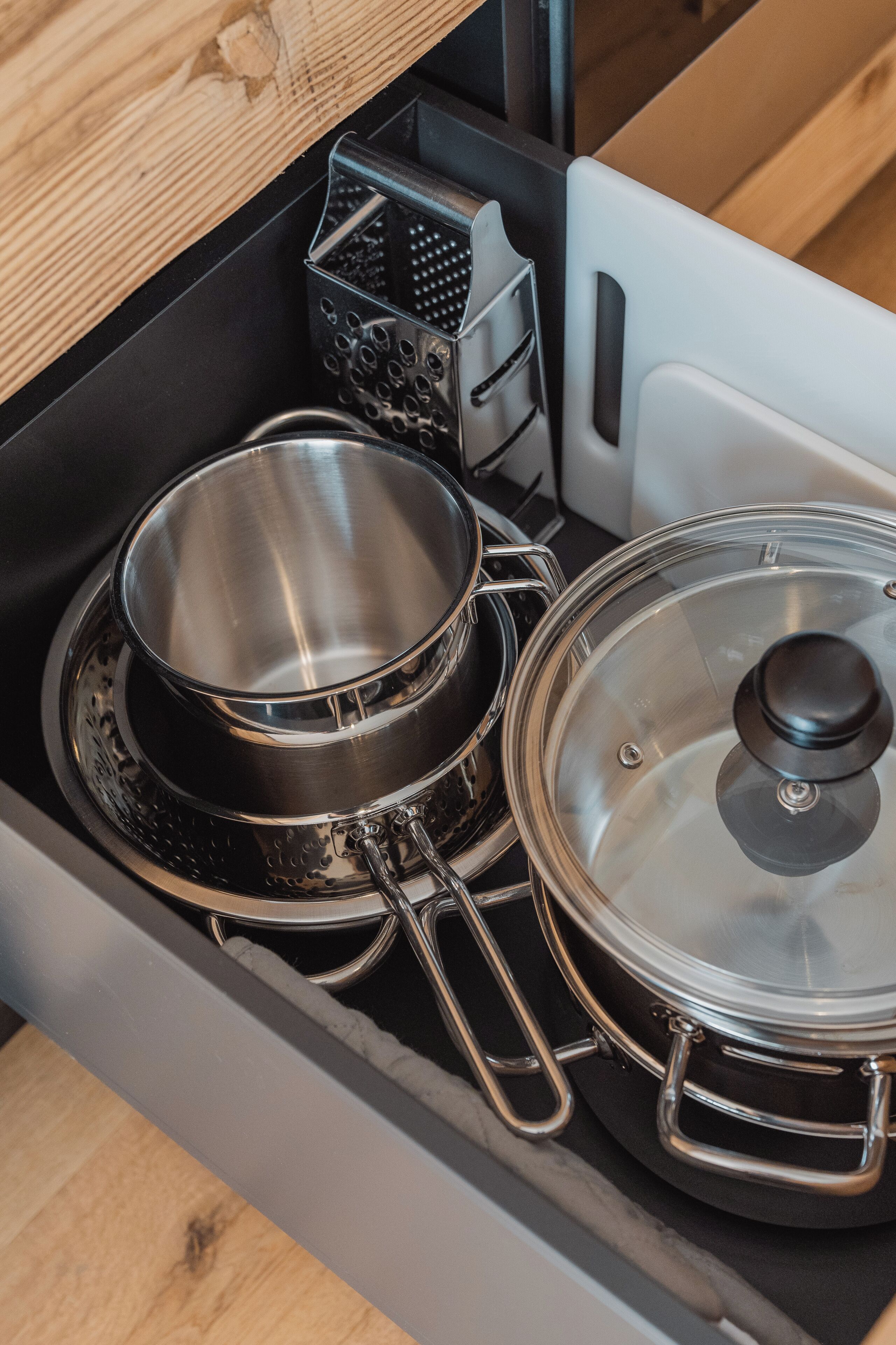 Uma gaveta de cozinha com utensílios de aço inoxidável, incluindo uma panela e uma frigideira, além de uma panela tampada.