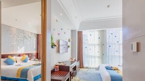 Quarto de hotel com cama, escrivaninha, cadeira, televisão e uma janela grande com cortinas.