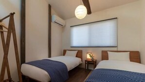 Quarto com duas camas, uma escada de madeira, uma mesa pequena com abajur e uma janela com persianas.