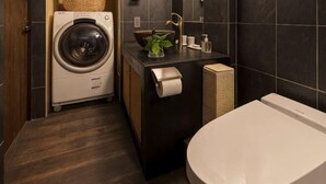 Uma casa de banho compacta com máquina de lavar roupa, lavatório com uma planta e sanita.
