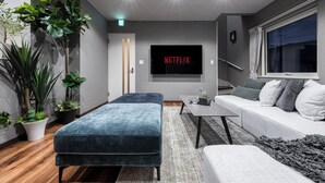 Uma sala de estar moderna com uma televisão de tela grande, um sofá, uma mesa de centro e um banquinho azul.