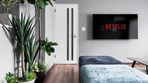 Quarto de hotel moderno com uma cama, televisão na parede e plantas em vasos.
