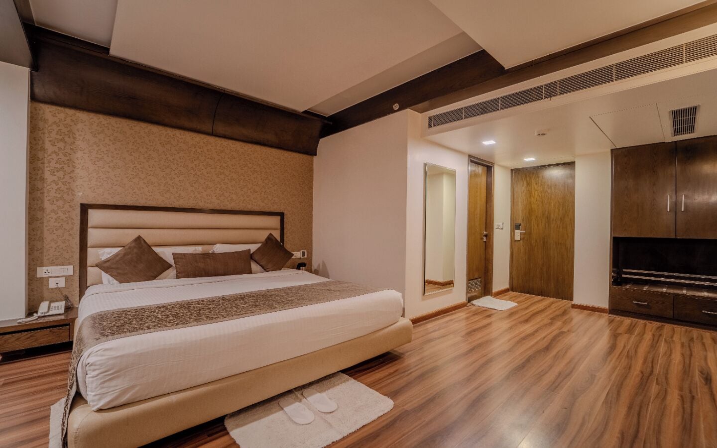 Quarto de hotel com uma cama grande, piso de madeira, televisão e guarda-roupa.
