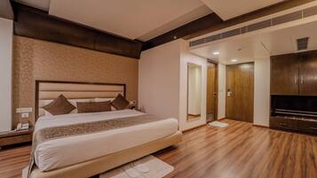 Quarto de hotel com uma cama grande, piso de madeira, televisão e guarda-roupa.