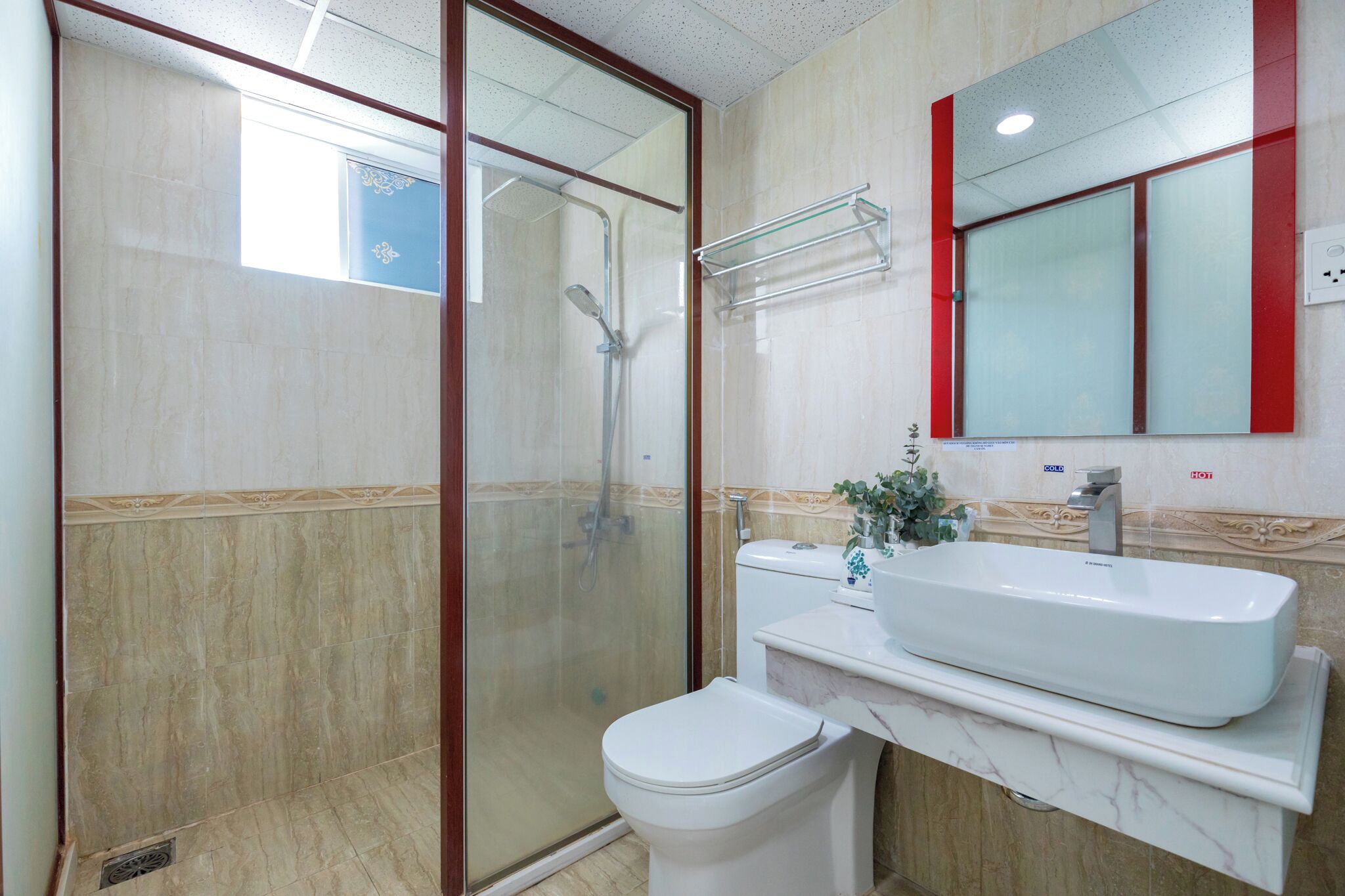Uma casa de banho moderna com cabine de duche em vidro, lavatório branco com bancada de mármore e sanita.