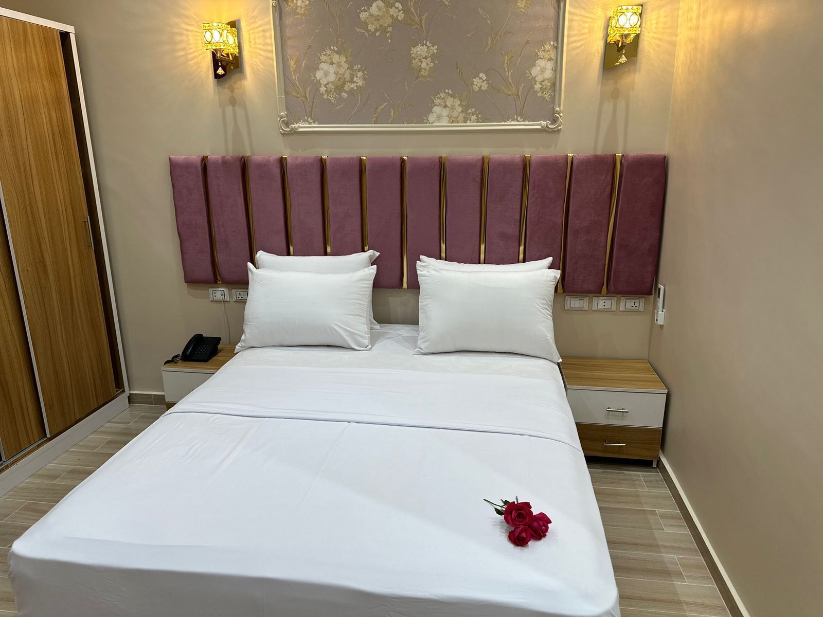 Quarto de hotel com cama, duas mesas de cabeceira, um criado-mudo, telefone e luminária fixa na parede.